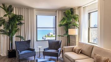 Sala de estar moderna com vista para o mar, dois poltronas, um sofá e uma mesa de centro.