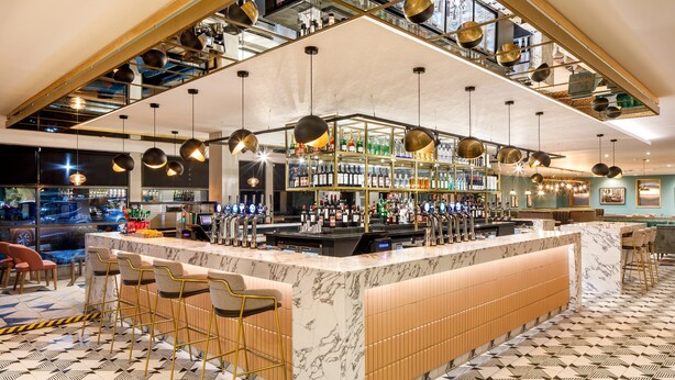 Uma área de bar com bancada de mármore, várias luminárias pendentes e chão estampado.