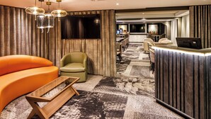 Um lobby de hotel moderno com área de estar, balcão de recepção e bar.