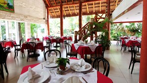 Restaurante com toalhas de mesa vermelhas, pratos brancos e cadeiras pretas.