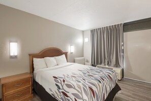 Quarto de hotel com cama, mesas de cabeceira, luminária na parede, janela com cortinas e ar condicionado de parede.