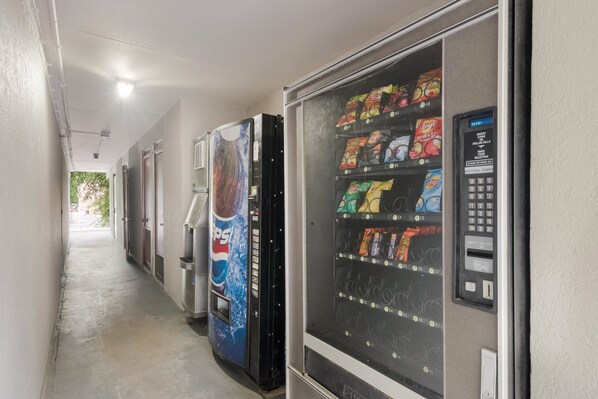Um corredor com máquinas de venda automática, incluindo um refrigerador de Pepsi e uma máquina com lanches e bebidas.