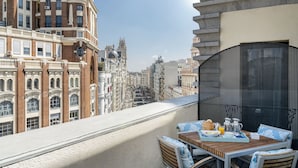 Uma varanda com mesa posta para o café da manhã, com vista para um horizonte urbano repleto de edifícios históricos.