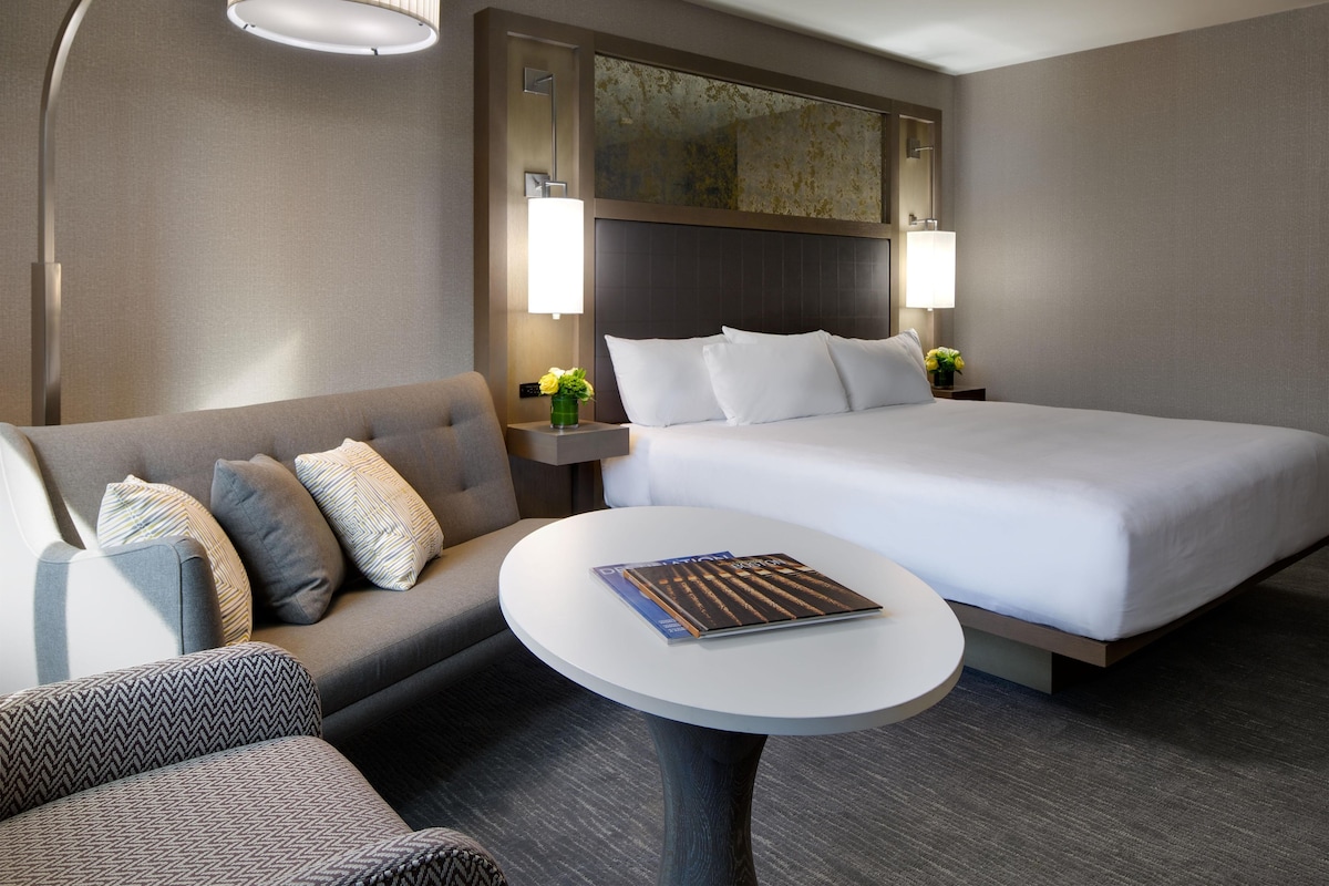 Quarto de hotel com cama, sofá, mesinha e abajur.