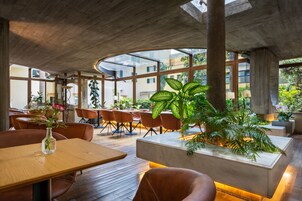 Um restaurante moderno com teto de concreto, grandes janelas e plantas em vasos.
