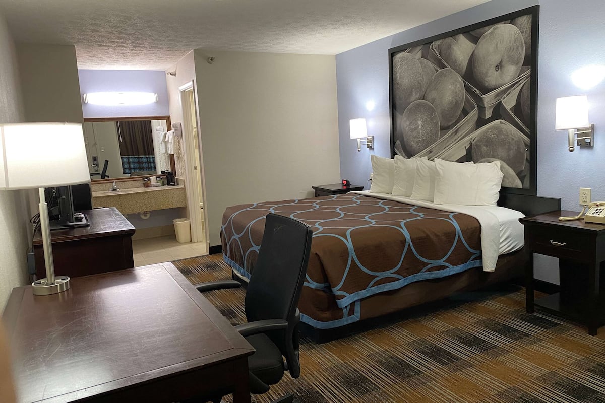 Quarto de hotel com cama, escrivaninha, cadeira e um espelho grande.