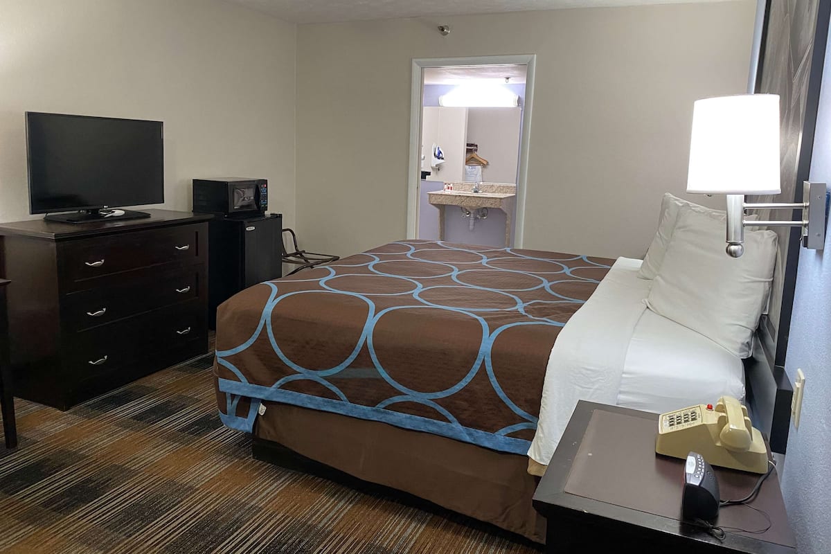 Quarto de hotel com cama, televisão, secretária com telefone e banheiro visível através de uma porta aberta.
