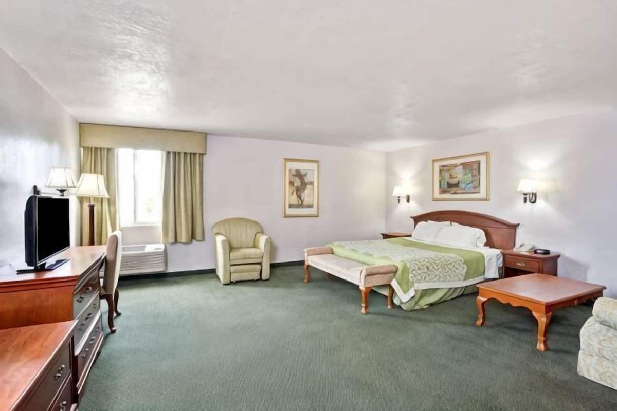Quarto de hotel com cama, escrivaninha, cadeira, televisão e duas luminárias na parede.