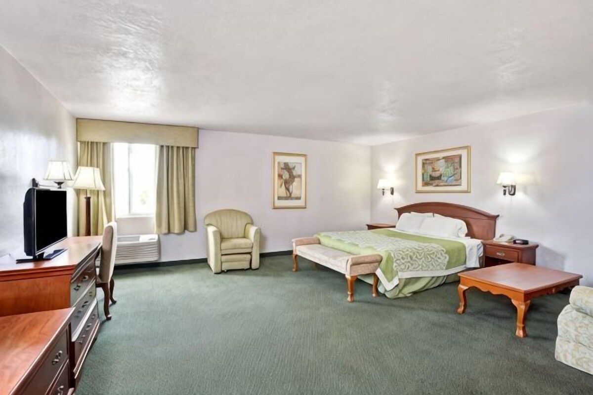 Quarto de hotel com cama, escrivaninha, cadeira, televisão e duas luminárias na parede.