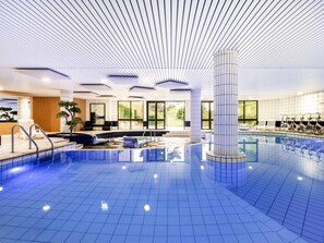 Piscina interior com piso ladrilhado, uma coluna grande e equipamentos de ginástica.