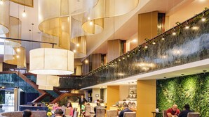 Um hall amplo com piso de mármore, lustres modernos e uma parede verde com plantas.