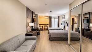 Quarto de hotel com duas camas, um sofá, uma escrivaninha, uma cadeira, uma televisão e um espelho.