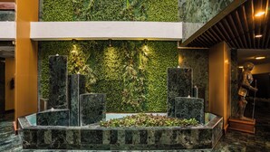 Um saguão com jardim vertical verde, colunas de mármore e uma estátua.