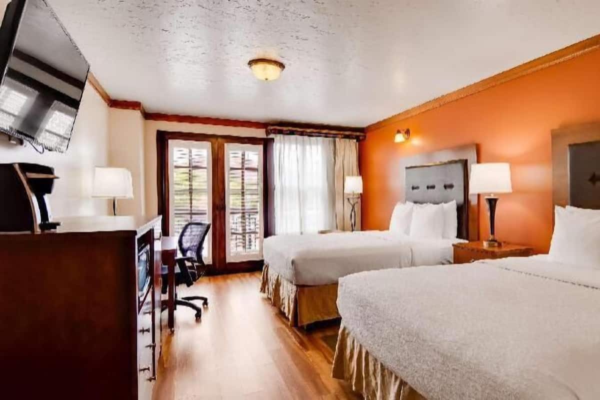 Quarto de hotel com duas camas, uma escrivaninha, uma cadeira, uma televisão e uma janela com cortinas.