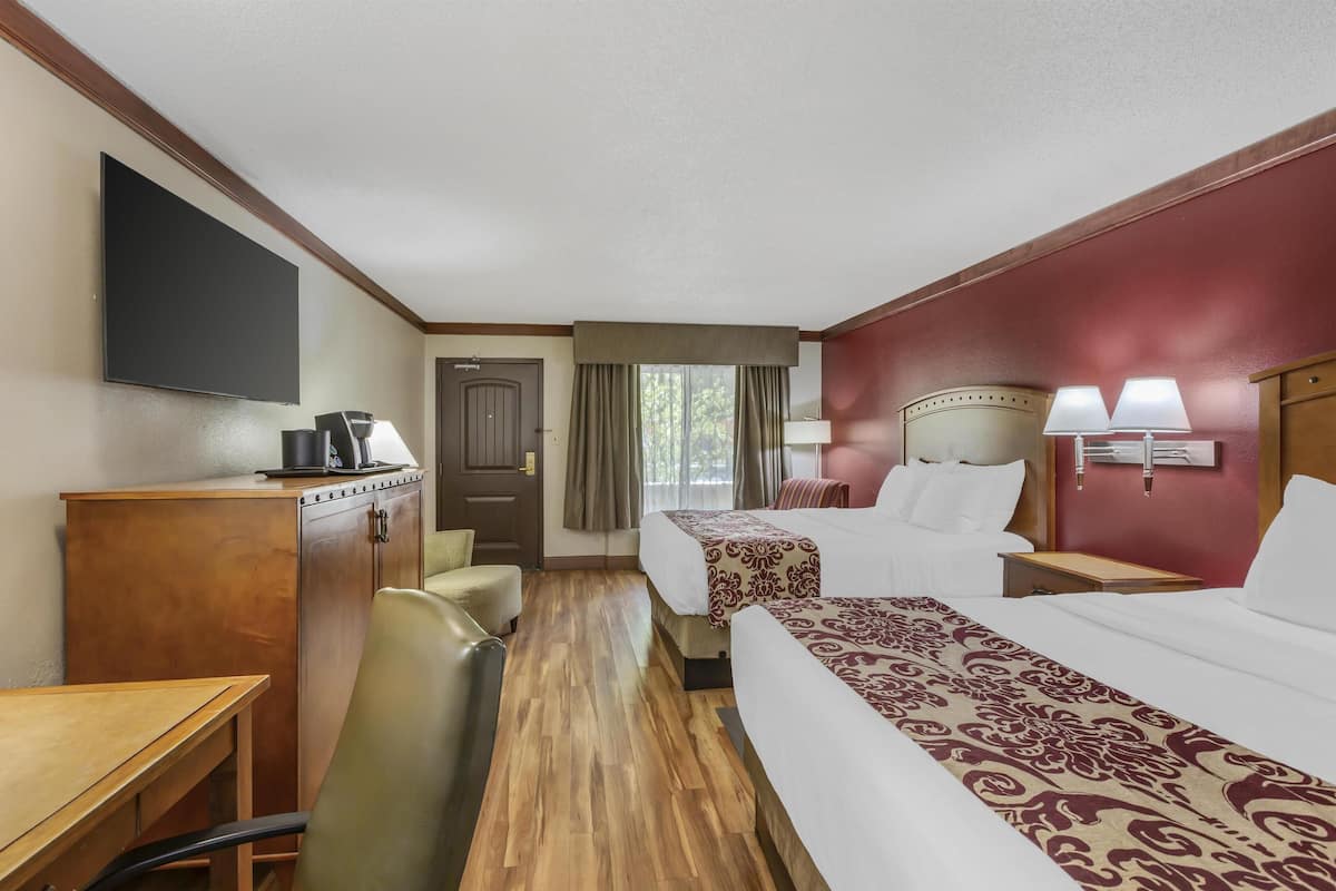 Quarto de hotel com duas camas, uma escrivaninha, uma cadeira, uma televisão e uma porta.
