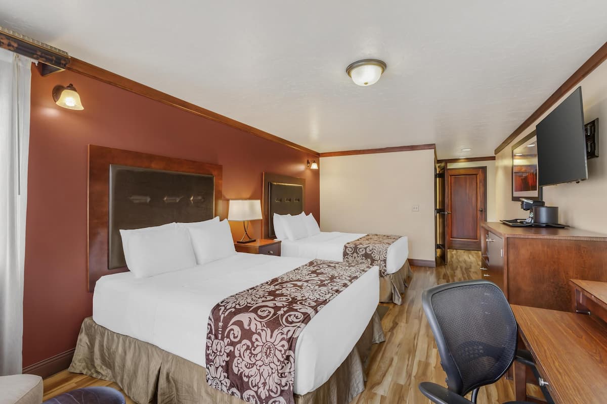 Quarto de hotel com duas camas, uma escrivaninha, uma cadeira, uma televisão e um armário de madeira.