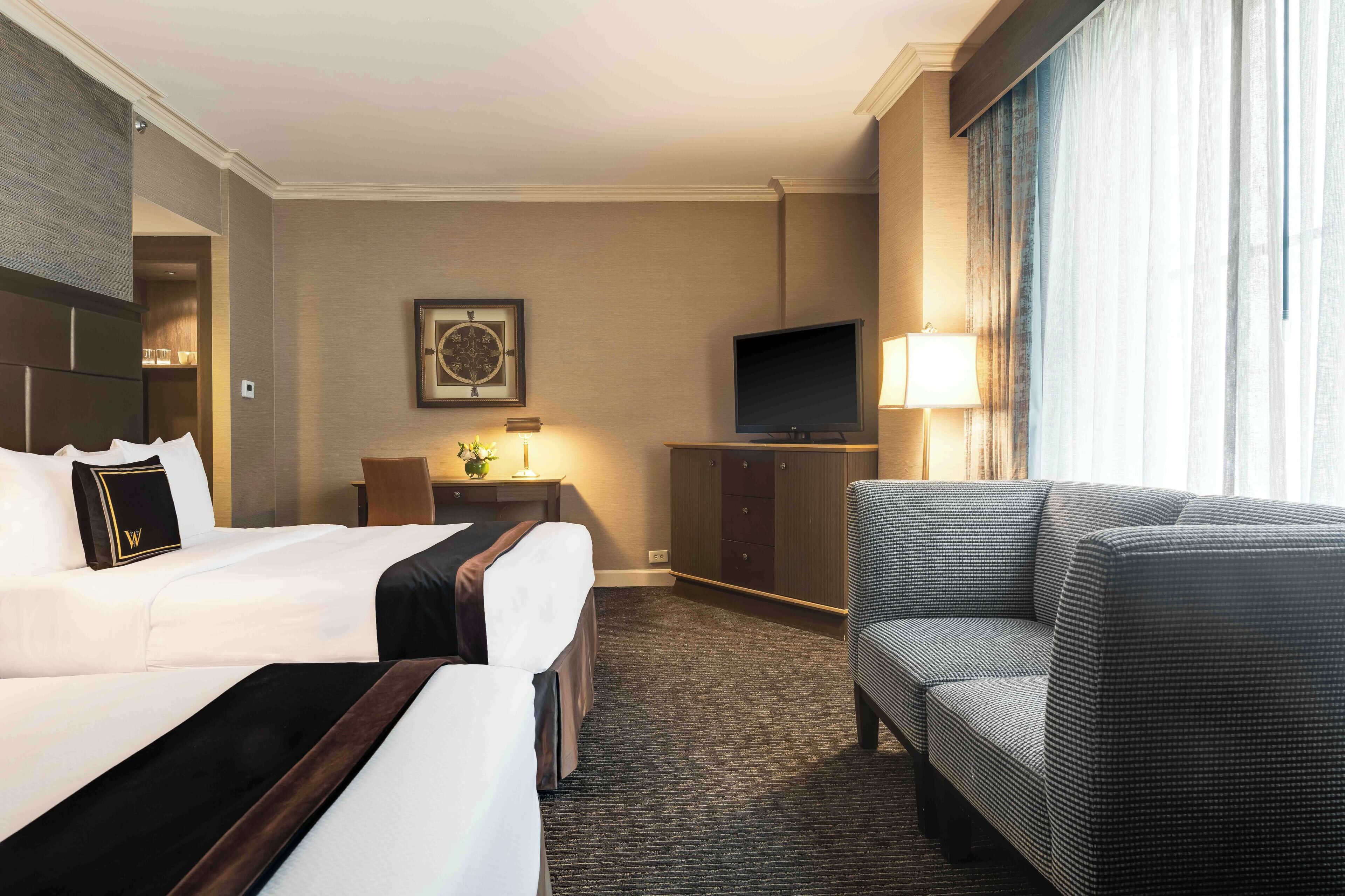 Quarto de hotel com uma cama grande, um sofá, uma televisão e uma escrivaninha com uma luminária.
