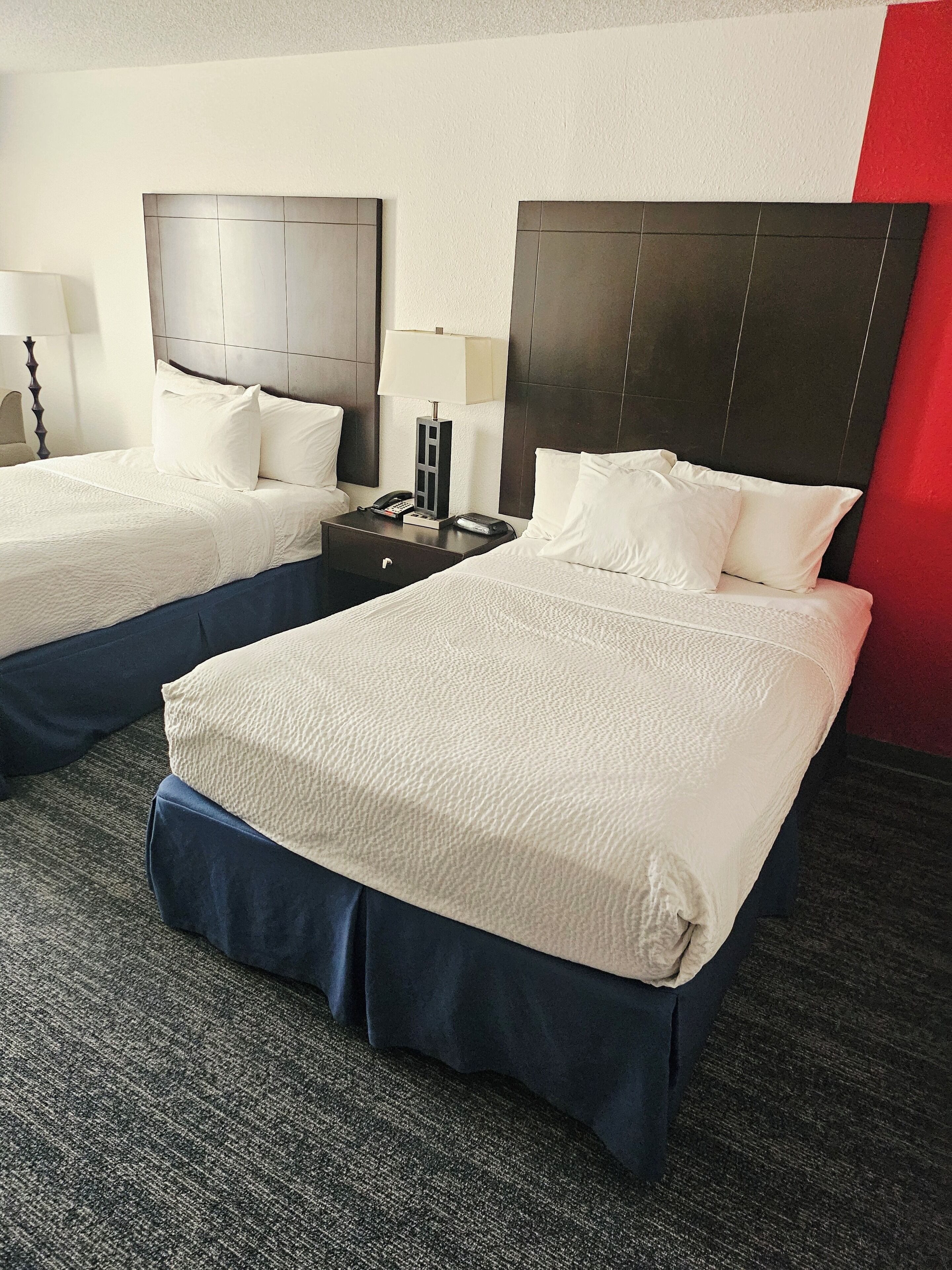 Quarto de hotel com duas camas, cada uma com cabeceira, mesa de cabeceira com abajur e telefone.