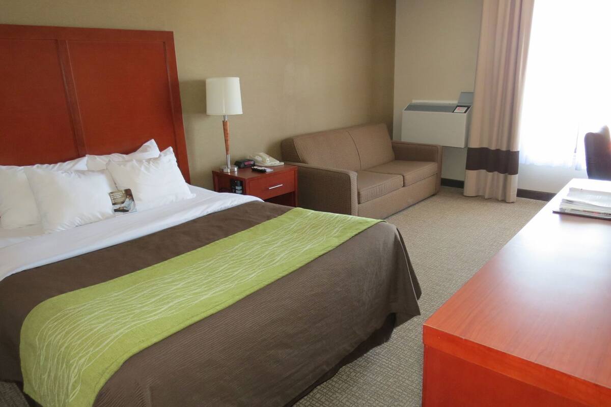 Quarto de hotel com uma cama, uma escrivaninha, uma cadeira, um abajur e um telefone.
