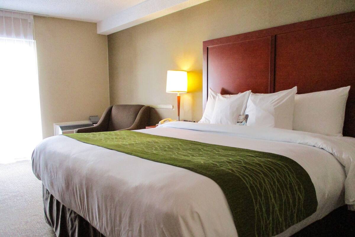 Quarto de hotel com uma cama grande, uma escrivaninha, uma cadeira e um abajur.