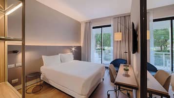 Quarto de hotel com cama grande, escrivaninha, cadeira, televisão e janela com cortinas.