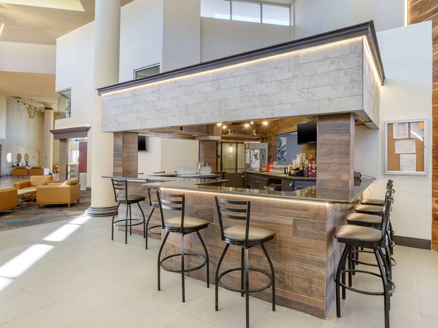 Uma área de bar moderna com balcão alto, banquetas e um espaço de estar com sofás e mesa de centro.