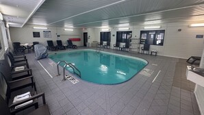 Uma piscina interior com chão de azulejos, cadeiras de espreguiçadeira e uma área de estar coberta.