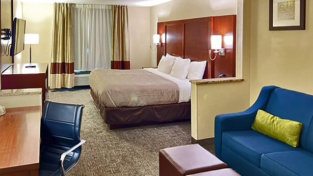 Quarto de hotel com cama, escrivaninha com cadeira, sofá azul e uma mesinha.