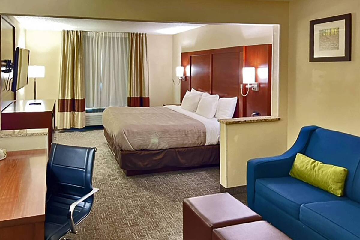 Quarto de hotel com cama, escrivaninha com cadeira, sofá azul e uma mesinha.