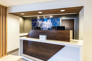 Balcão de recepção com design moderno, destacando um painel frontal de madeira e um padrão geométrico azul no fundo.