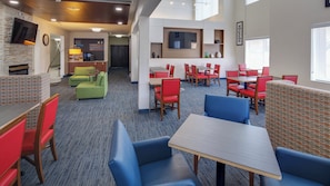 Um lobby de hotel moderno com áreas de estar, um espaço para café e uma TV fixada na parede.