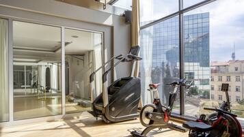 Uma academia moderna com equipamentos de cardio, uma janela ampla com vista para a cidade e uma porta de vidro que dá para outro espaço.