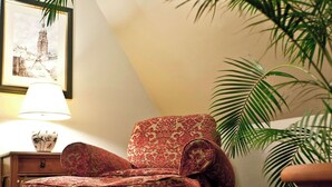 Quarto de canto com uma poltrona estampada vermelha, um vaso de planta e uma luminária em uma mesa de cabeceira.