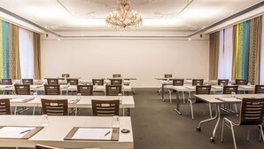 Uma sala de conferências com fileiras de mesas e cadeiras, um candelabro e cortinas estampadas.