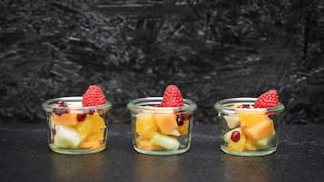 Três recipientes de vidro com salada de frutas, cada um com uma morango e um framboesa, sobre uma superfície escura.