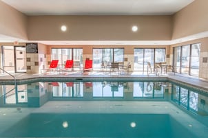 Piscina interna com paredes de vidro transparente, cadeiras vermelhas e uma mesa com cadeiras.