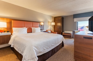 Quarto de hotel com uma cama grande, uma escrivaninha, uma cadeira e um guarda-roupa.
