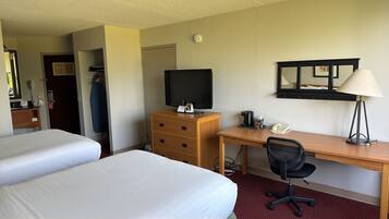 Quarto de hotel com duas camas, uma escrivaninha com cadeira, televisão, luminária e telefone.