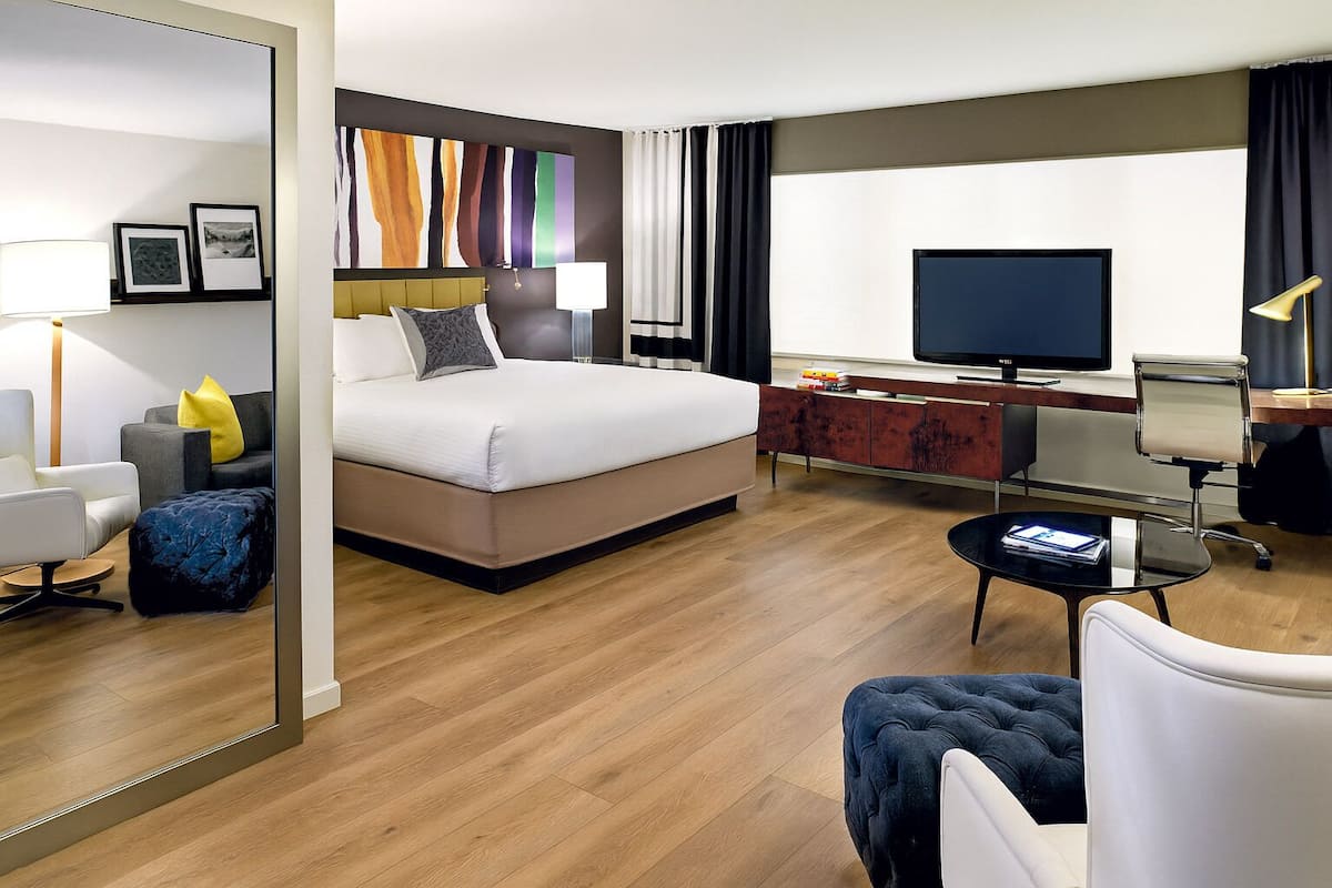 Quarto de hotel moderno com uma cama grande, uma escrivaninha, uma TV e uma área de estar.