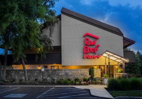Um hotel Red Roof Plus com fachada moderna, parede de pedra e estacionamento.