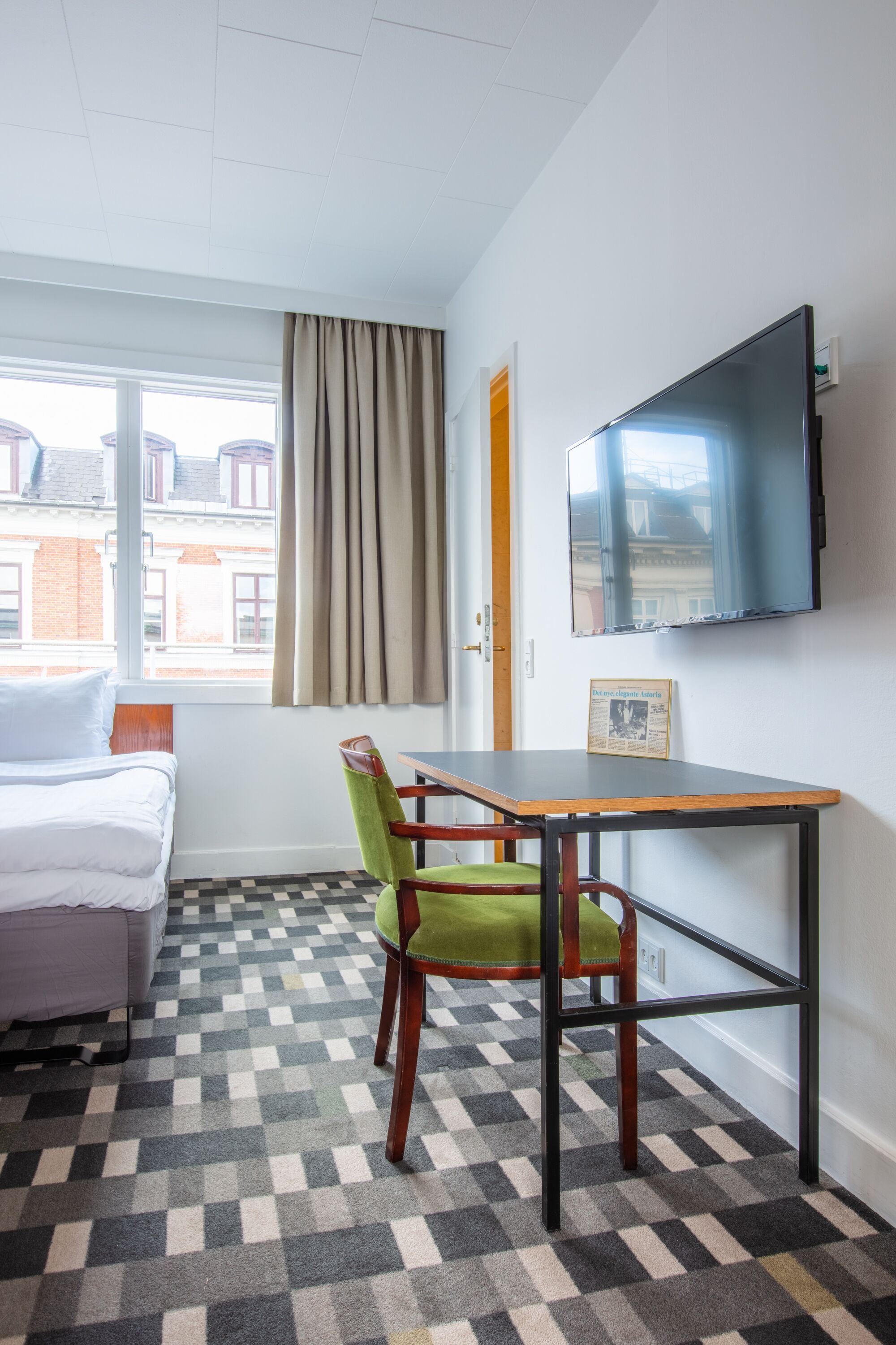 Quarto de hotel com cama, mesa, cadeira, televisão e janela com cortinas.