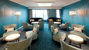 Quarto de hotel com carpete azul, dois sofás, quatro poltronas, duas mesinhas redondas e luminárias de chão.