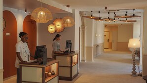 Uma área de recepção com balcão, dois recepcionistas e corredor com iluminação decorativa.