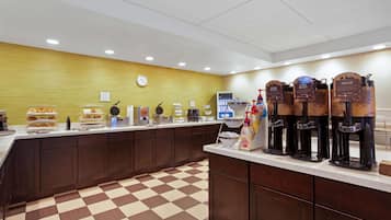 Espaço de café da manhã em hotel, com chão quadriculado, parede de madeira e balcão com máquinas de café e dispensador de bebidas.