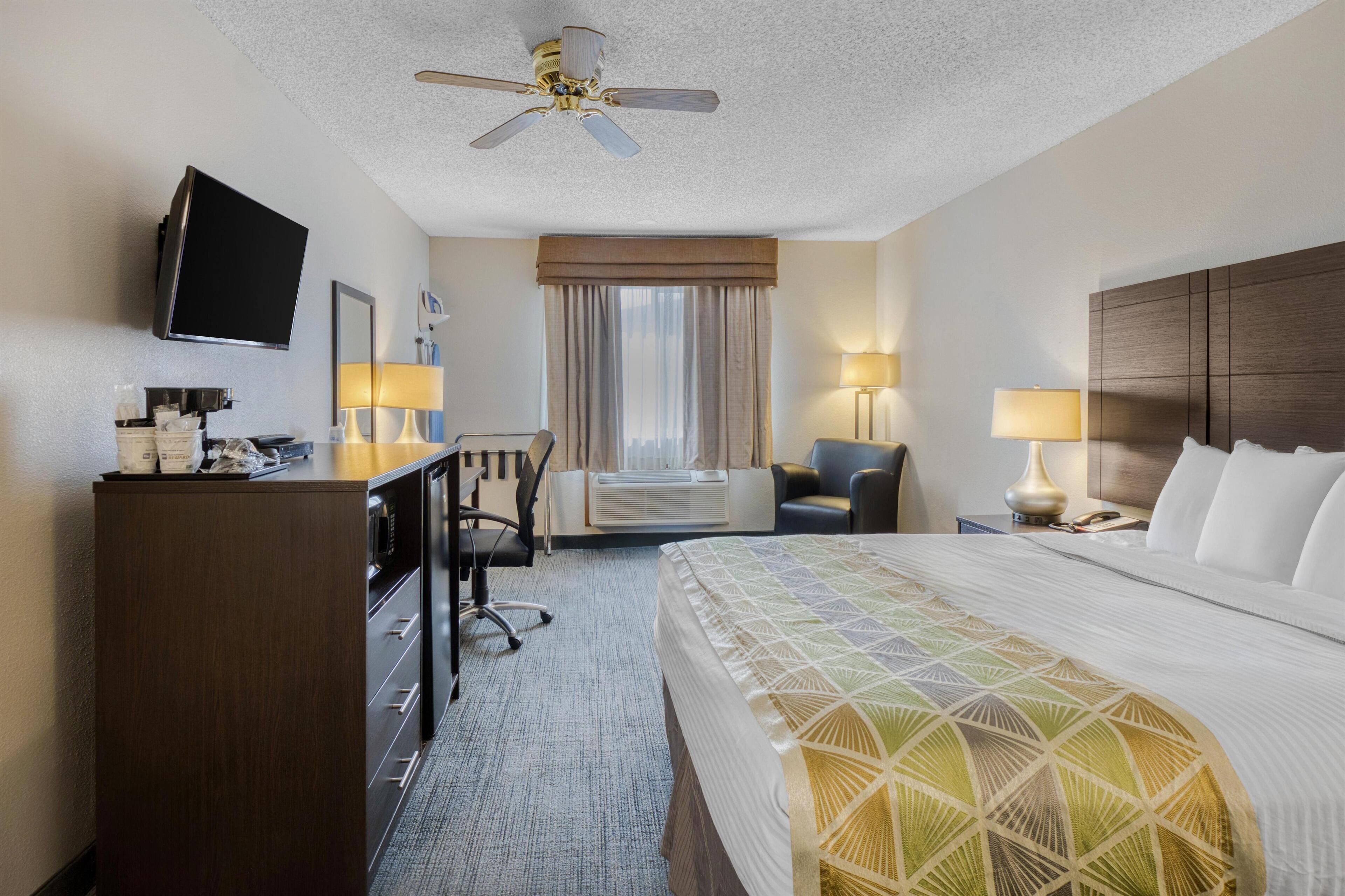 Quarto de hotel com cama, escrivaninha, cadeira e televisão.