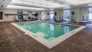 Piscina interior com água cristalina, rodeada por espreguiçadeiras e teto com iluminação embutida.