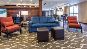 Um hall de hotel com um sofá azul, poltronas vermelhas e um tapete estampado.