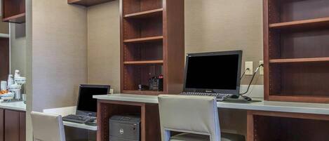 Quarto de hotel com escrivaninha, duas cadeiras, impressora e computador.