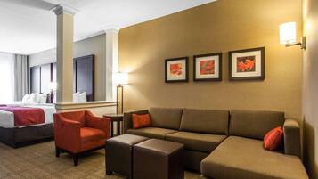 Quarto de hotel com cama, sofá, duas poltronas, mesa de centro e parede com três quadros emoldurados.