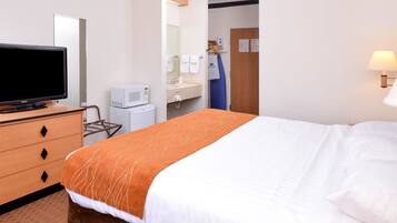 Quarto de hotel com cama, televisão, micro-ondas, cômoda e banheiro visível por uma porta aberta.